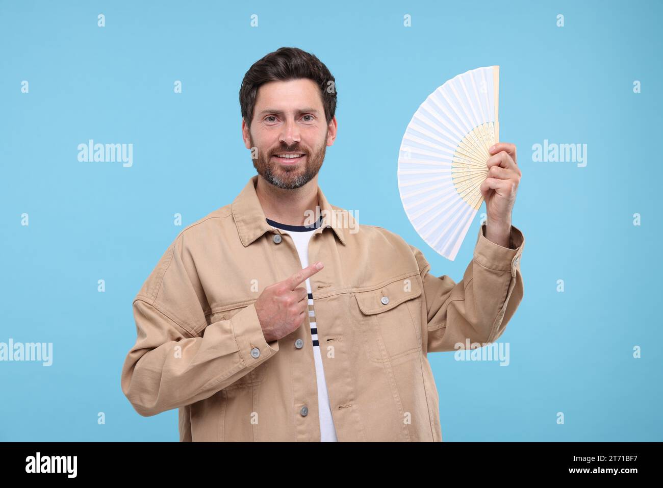 Happy man holding hand fan on light blue background Stock Photo - Alamy