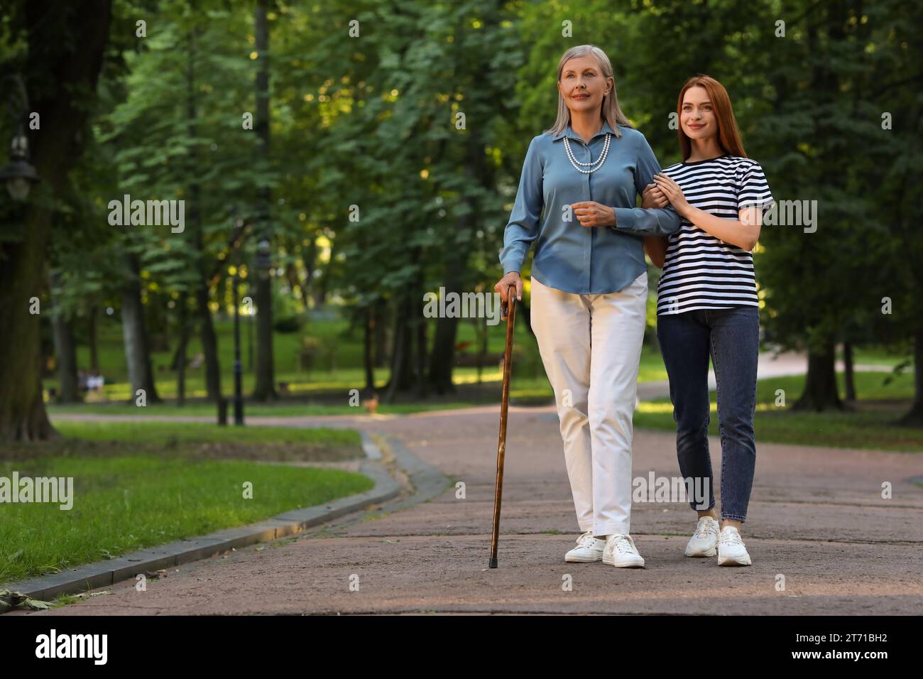 Senior lady with walking cane and young woman in park. Space for text ...