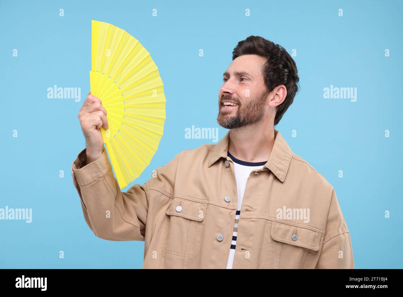 Happy man holding hand fan on light blue background Stock Photo - Alamy