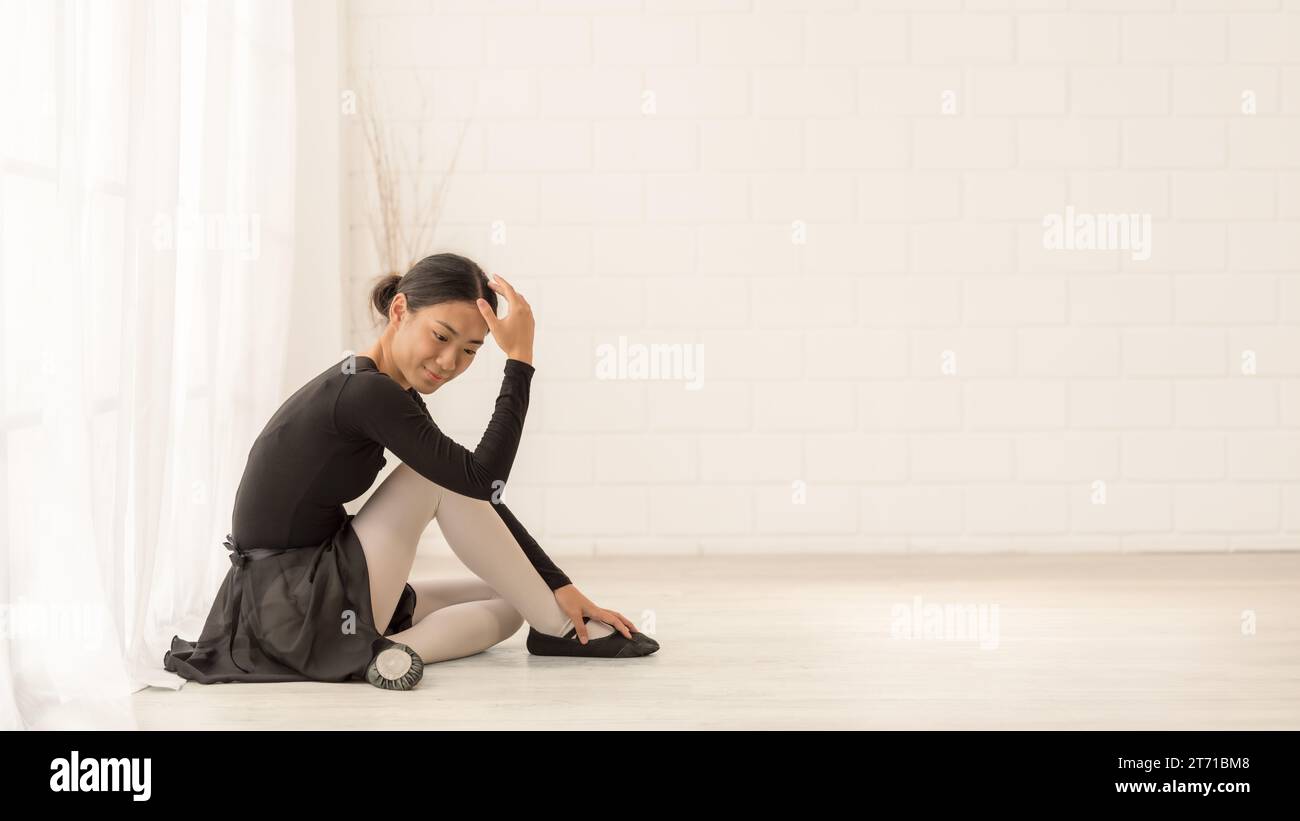 An Asian ballet dancer exudes calm as she relaxes on a studio floor, a ...