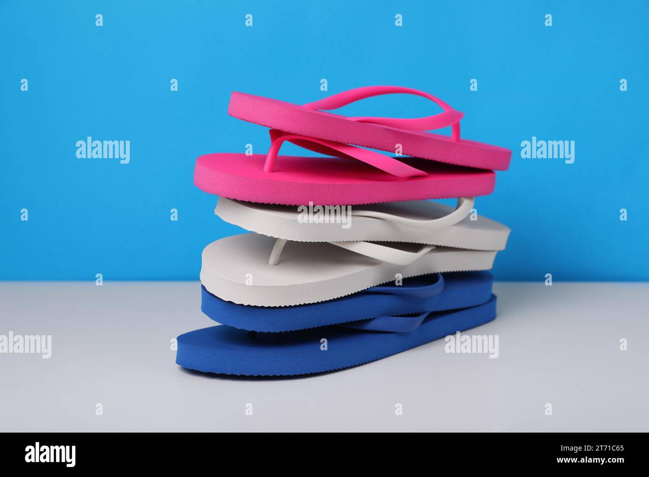 Stack of different flip flops on white table against light blue ...