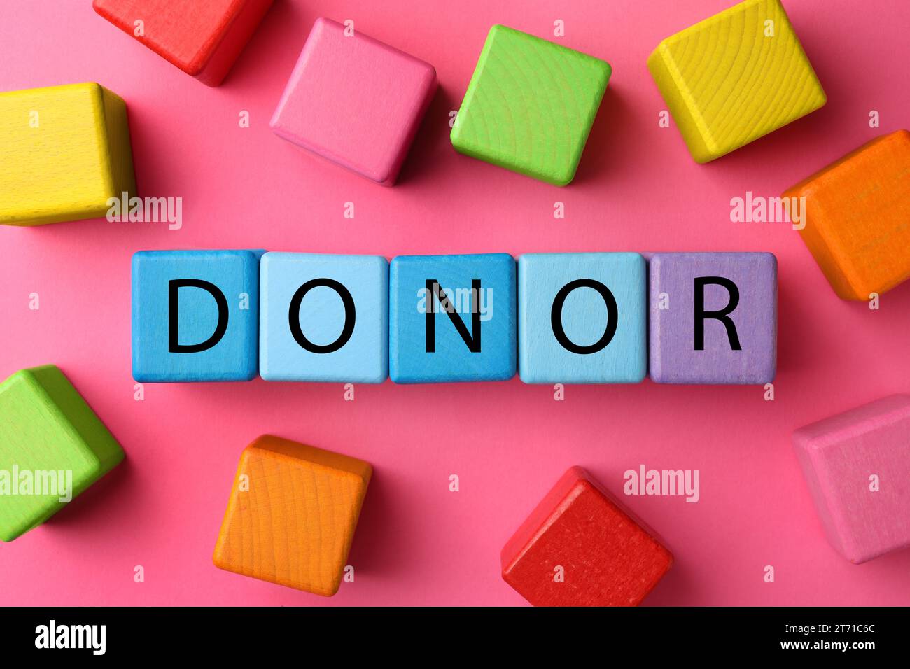 Word Donor made of colorful wooden cubes on pink background, flat lay ...