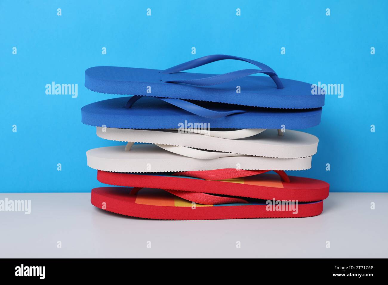 Stack of different flip flops on white table against light blue ...