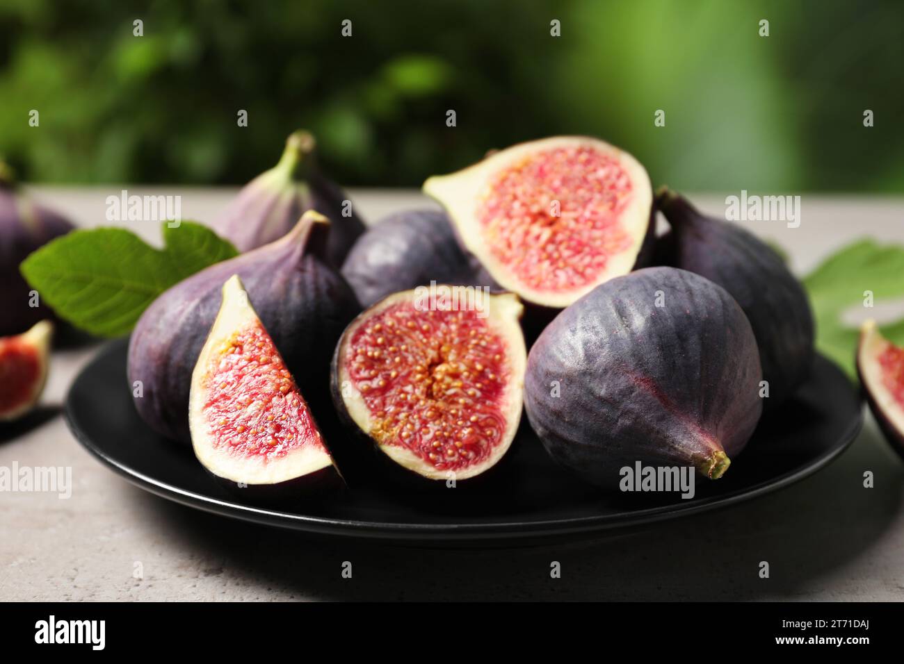 Whole and cut ripe figs on light grey table against blurred green ...