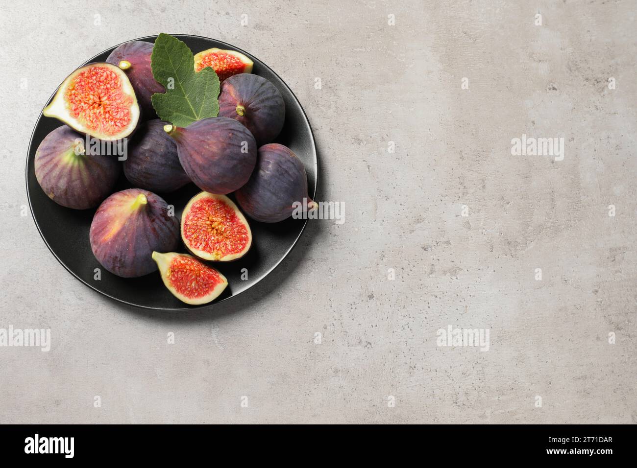 Whole and cut ripe figs with leaf on light grey textured table, top ...