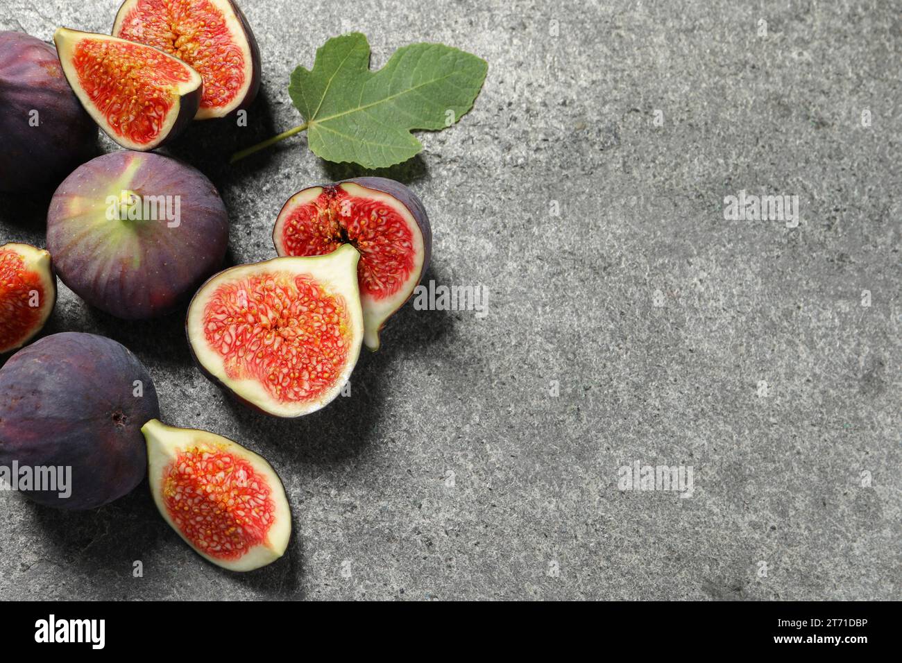 Whole and cut ripe figs with leaf on grey textured table, flat lay ...