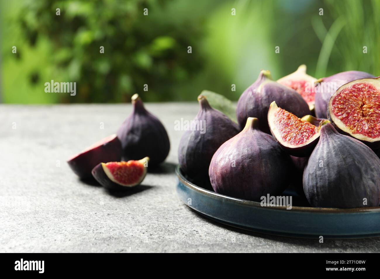 Whole and cut ripe figs on light grey textured table against blurred ...