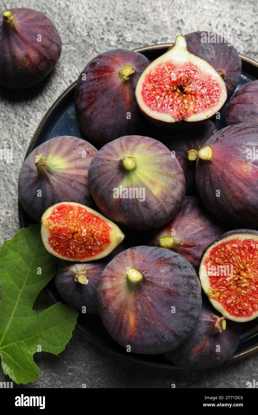Whole and cut ripe figs with leaf on light grey textured table, flat ...