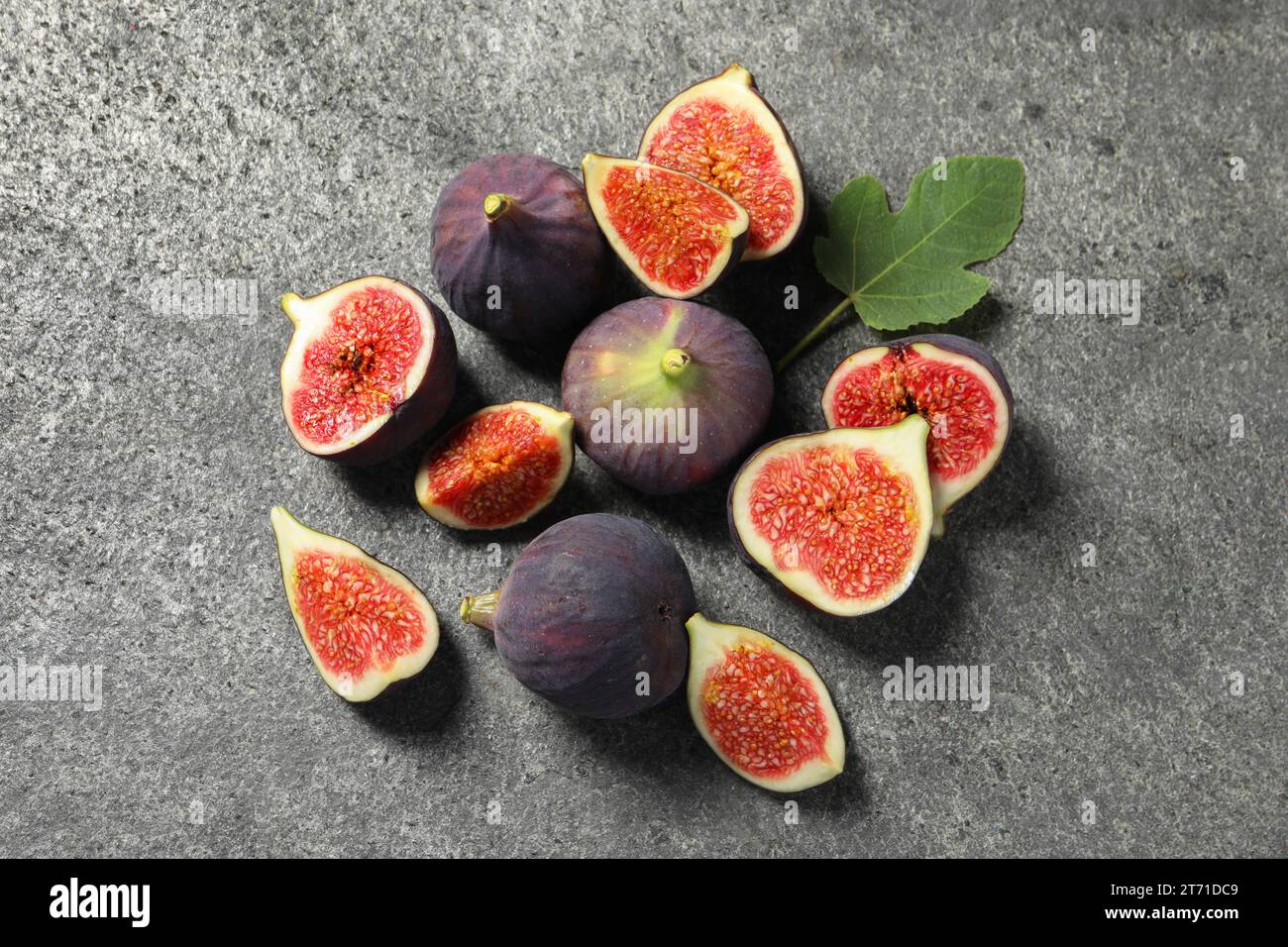 Whole and cut ripe figs with leaf on grey textured table, flat lay ...