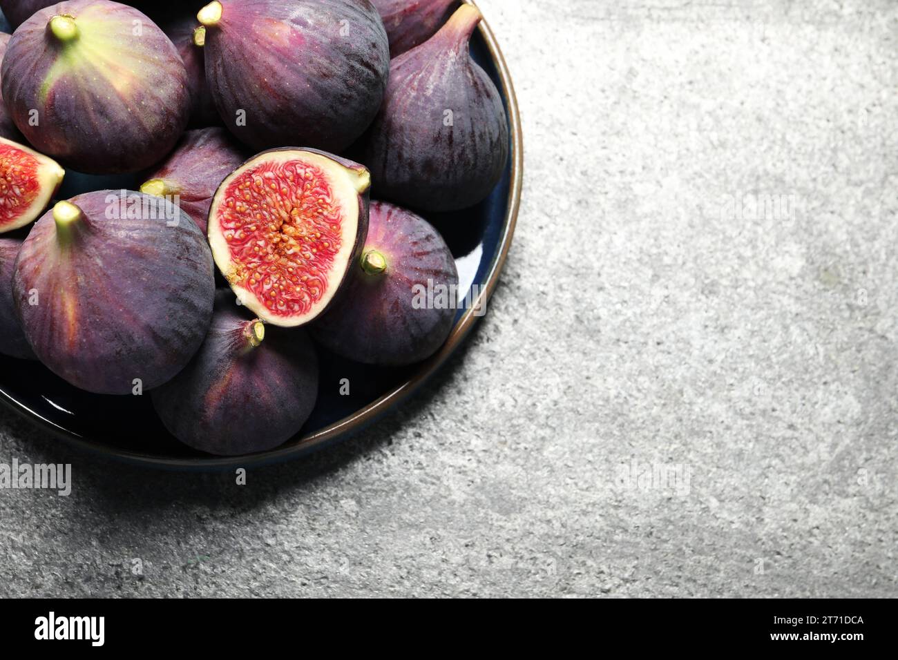 Whole and cut ripe figs on light grey textured table, top view. Space ...