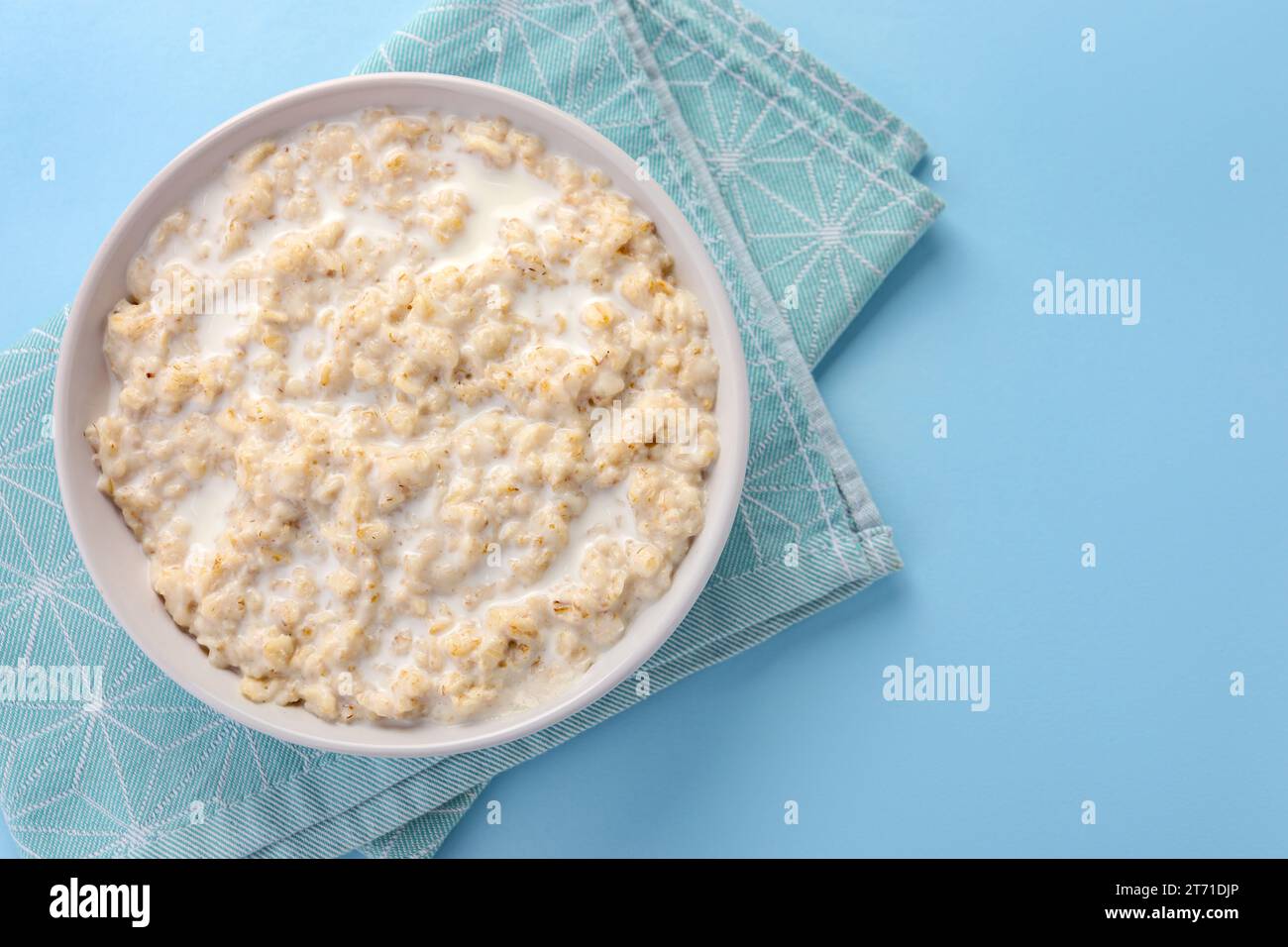Tasty boiled oatmeal in bowl on light blue table, top view. Space for ...