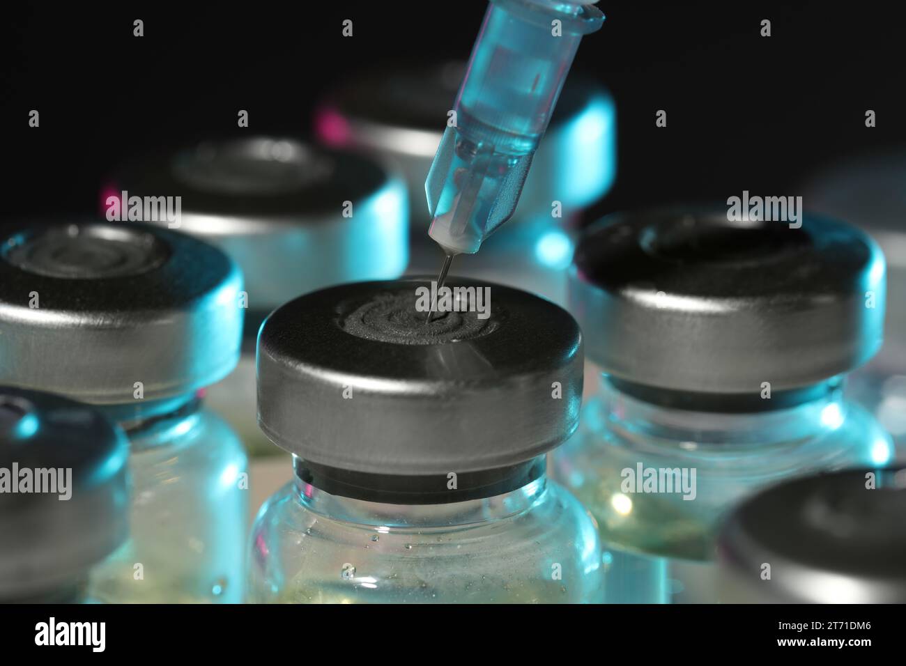 Filling syringe with medicine from vial against dark background ...