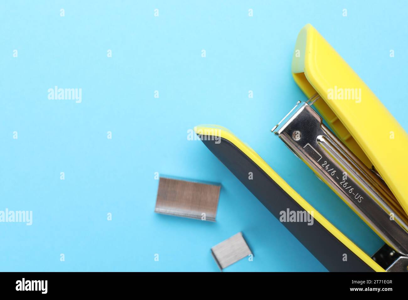 Yellow stapler with staples on light blue background, top view. Space ...