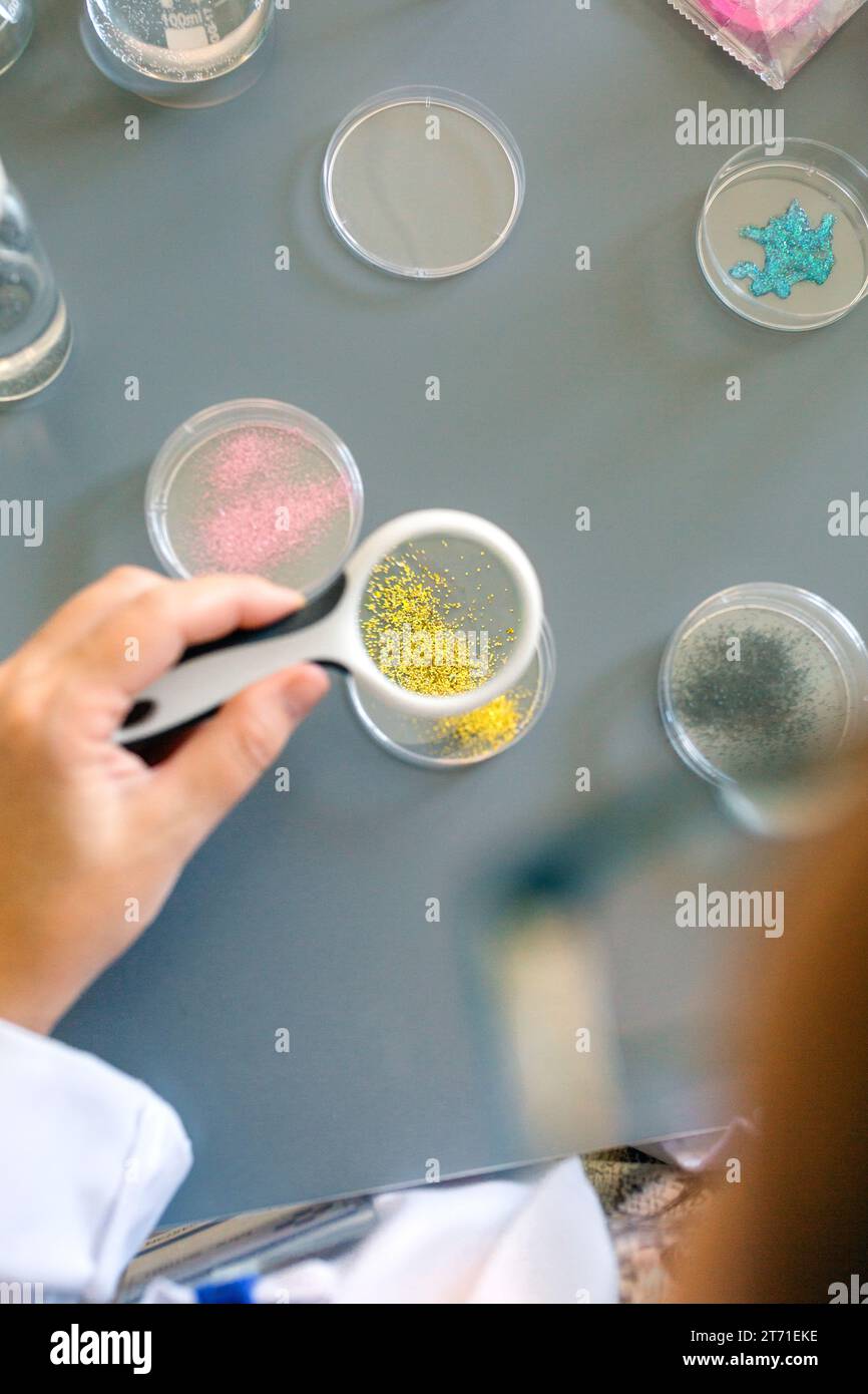 Female scientist examining golden glitter sample through a magnifying ...