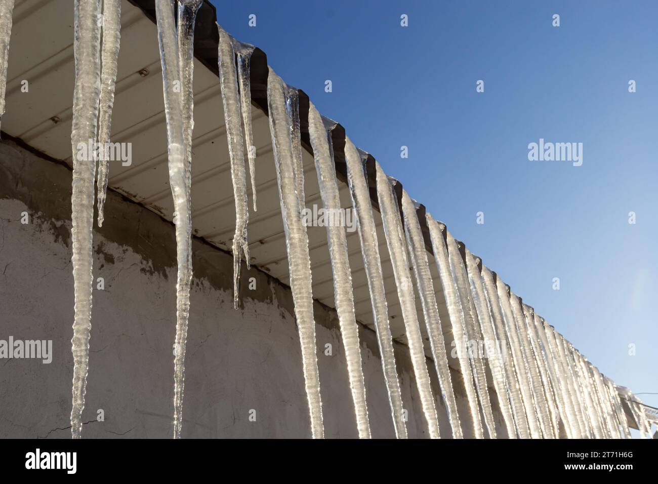 Sharp icicles and melted snow hanging from the eaves of the roof ...