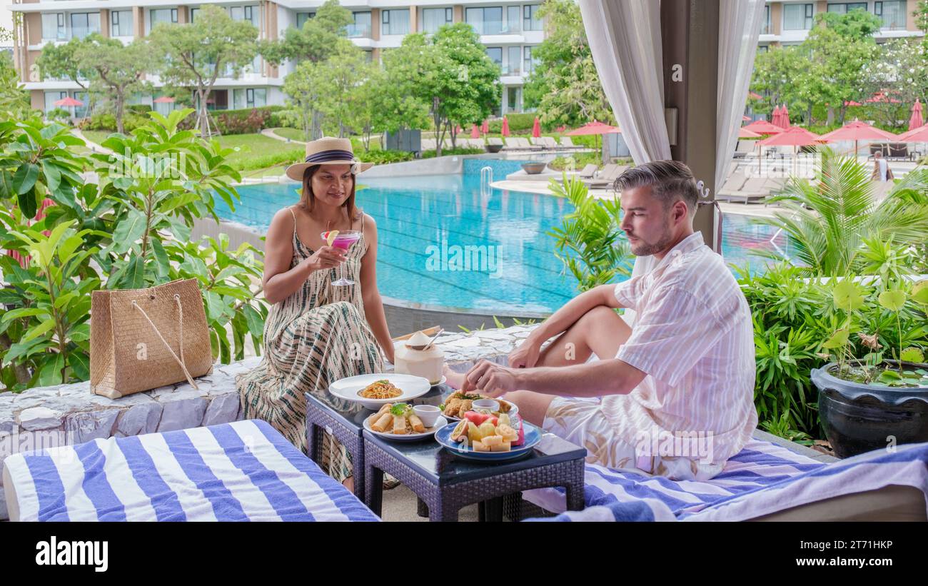 couple having lunch at a restaurant looking out over the swimming pool ...