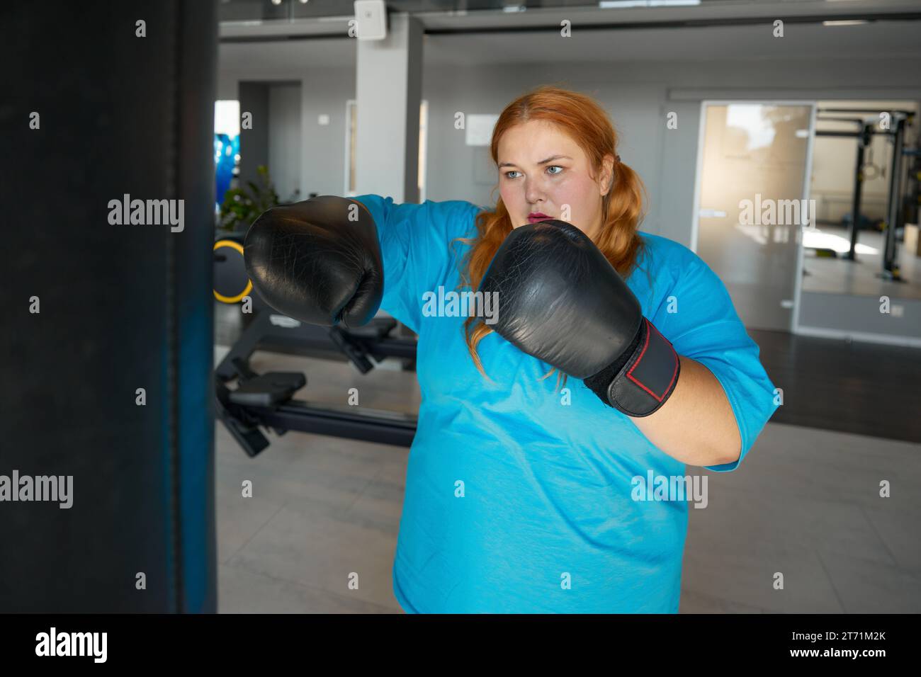 Concentrated fat woman using boxing gloves doing punching exercises ...