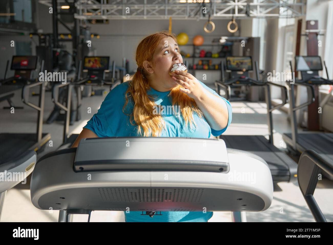 Front view on funny obese woman eating cake while training on treadmill ...