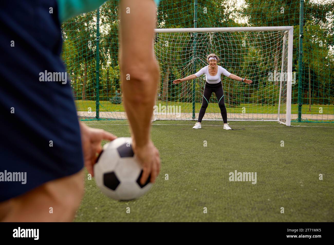 Elderly woman standing at gates getting ready to catch soccer ball ...