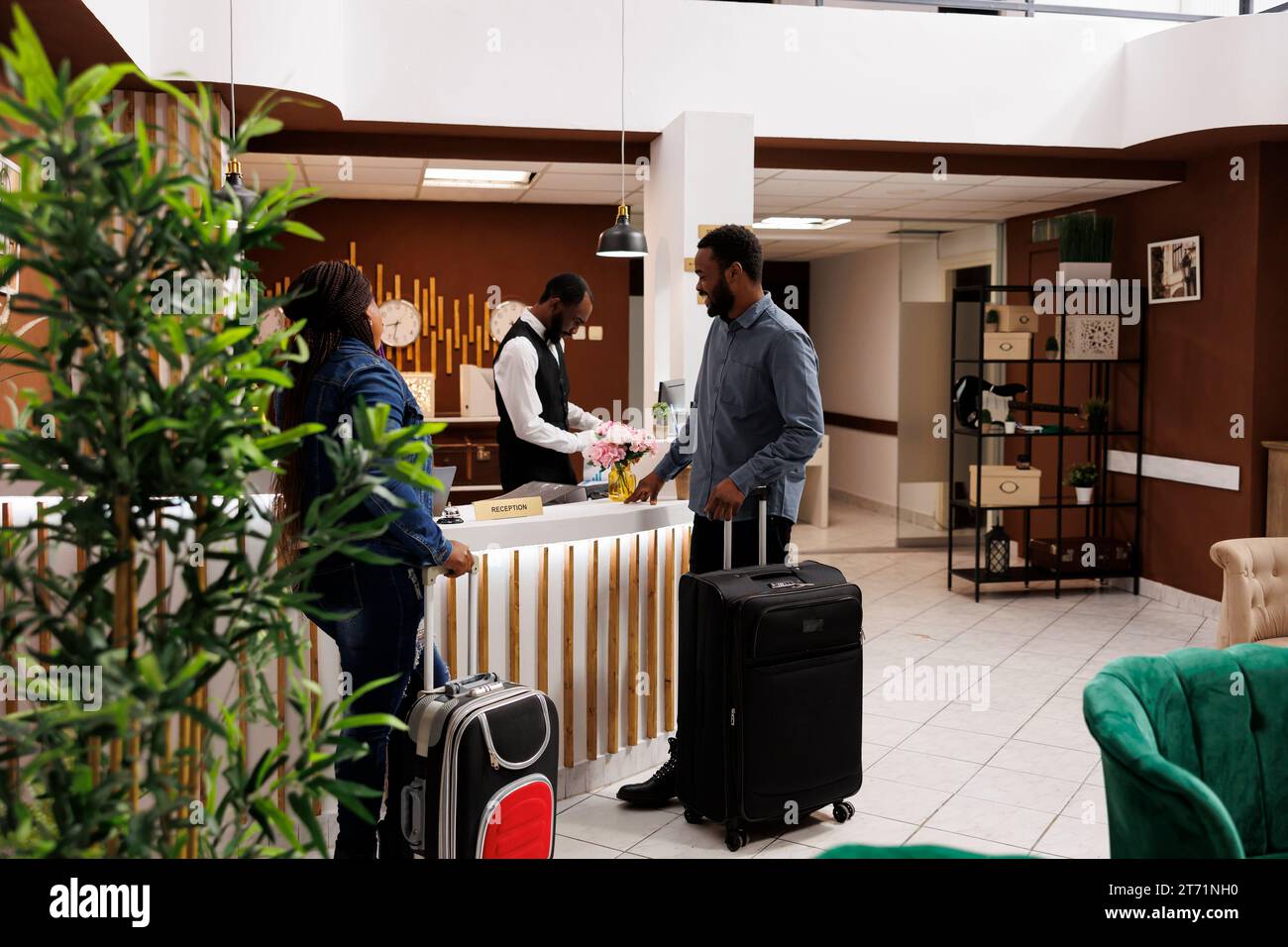 Happy black couple standing at hotel front desk with luggage, checking ...