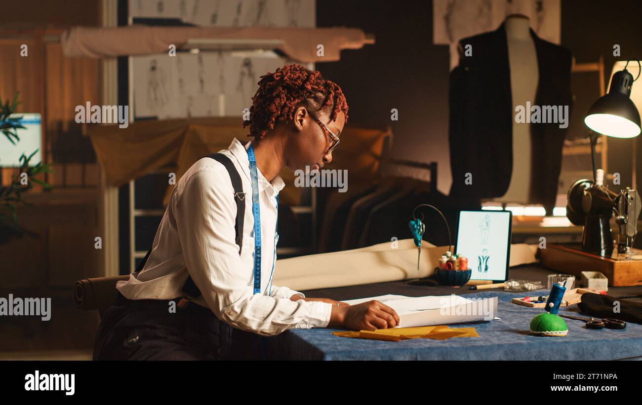 Fashion designer works on clothing items, looking at sketches to create ...