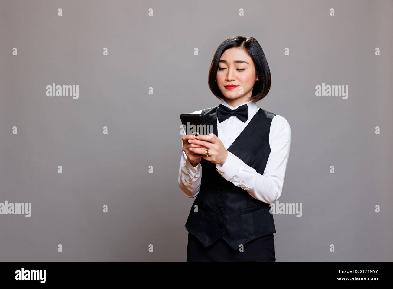 Smiling asian restaurant waitress in black and white uniform typing ...
