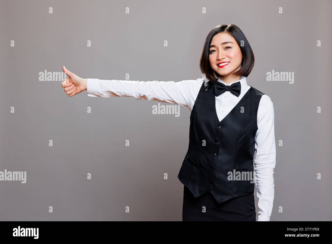 Smiling asian waitress showing thumb up gesture and looking at camera ...