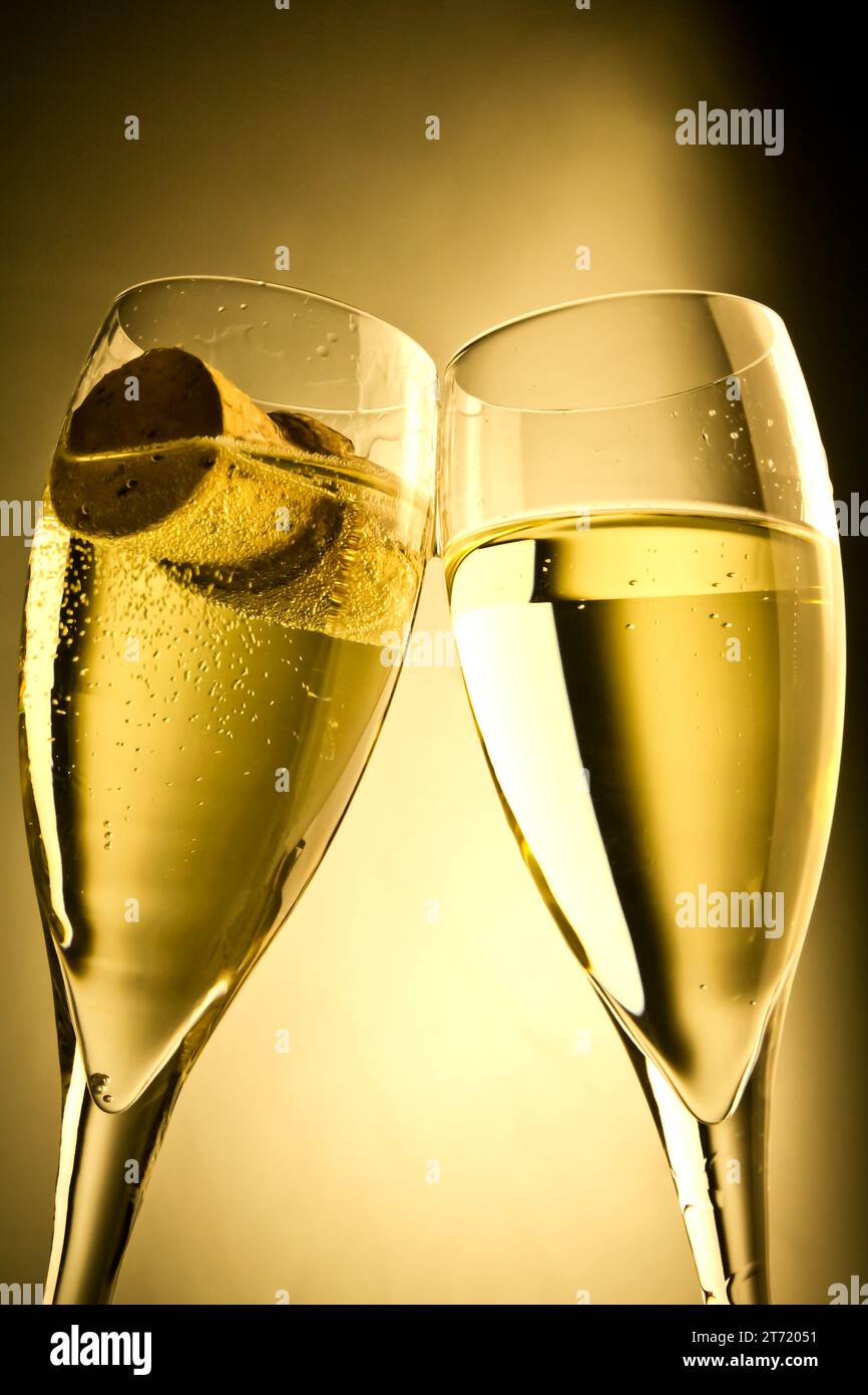 close up a pair of champagne flutes with bottle cap against a golden ...