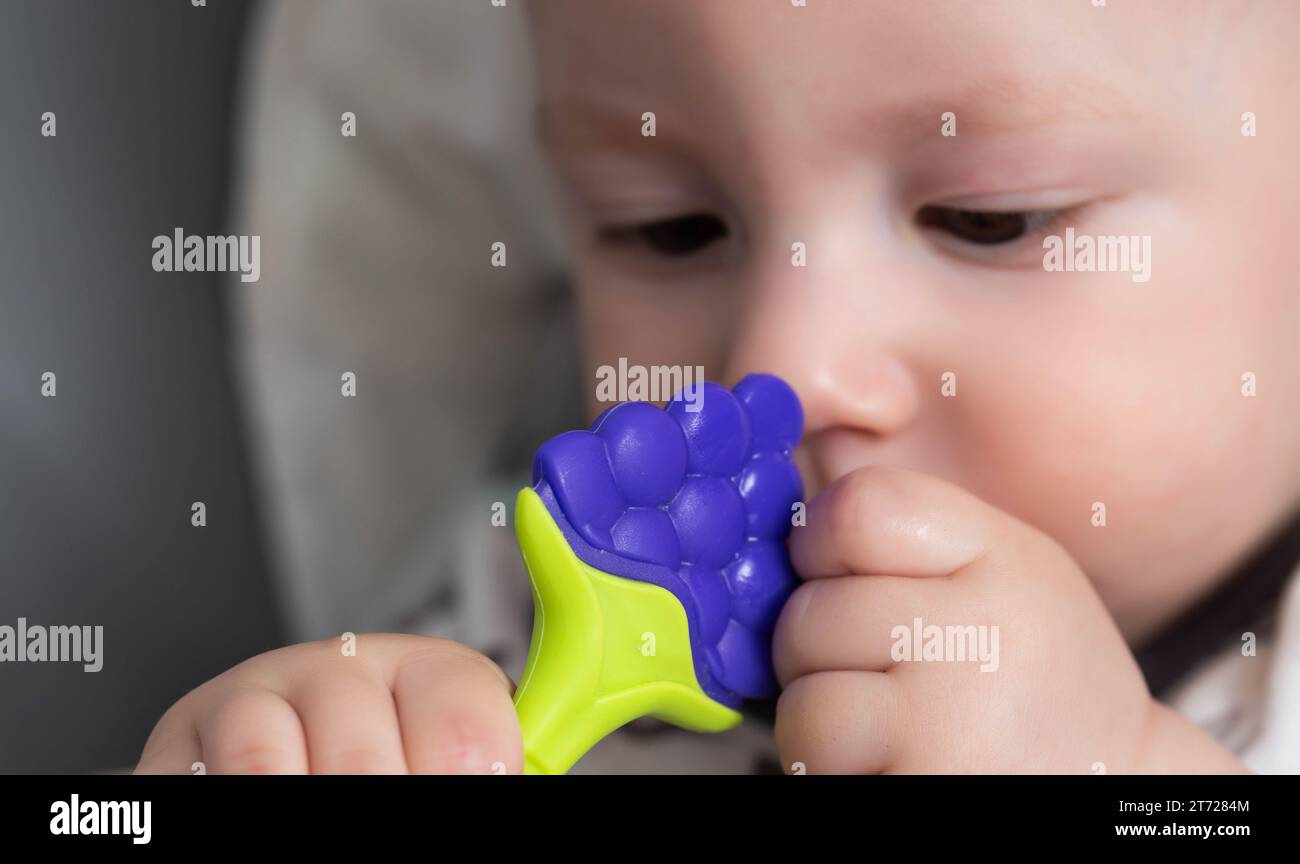 Handsome baby boy bites with his mouth a silicone massager with cooling ...
