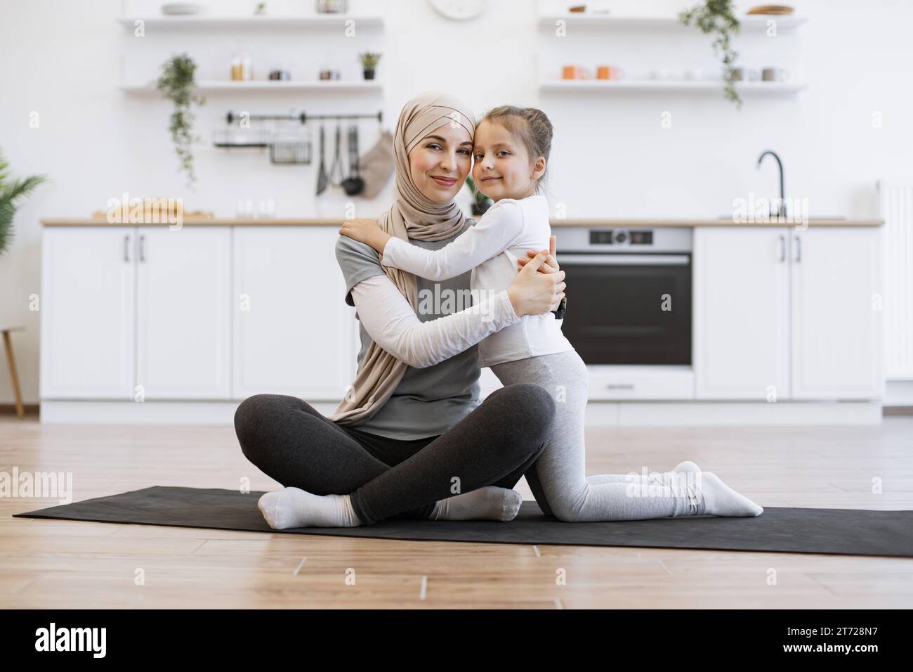 Loving muslim female in hijab hugging daughter during fitness routine ...