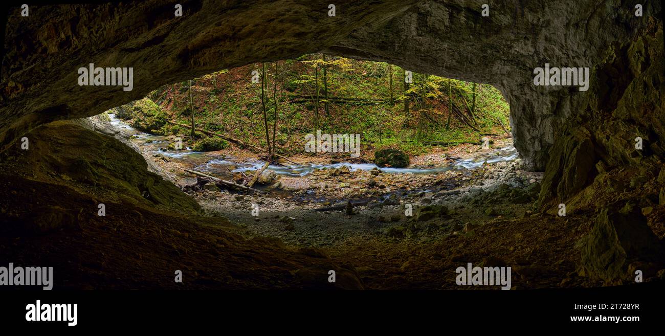 Vibrant autumnal landscape of a large cave entrance with a river ...