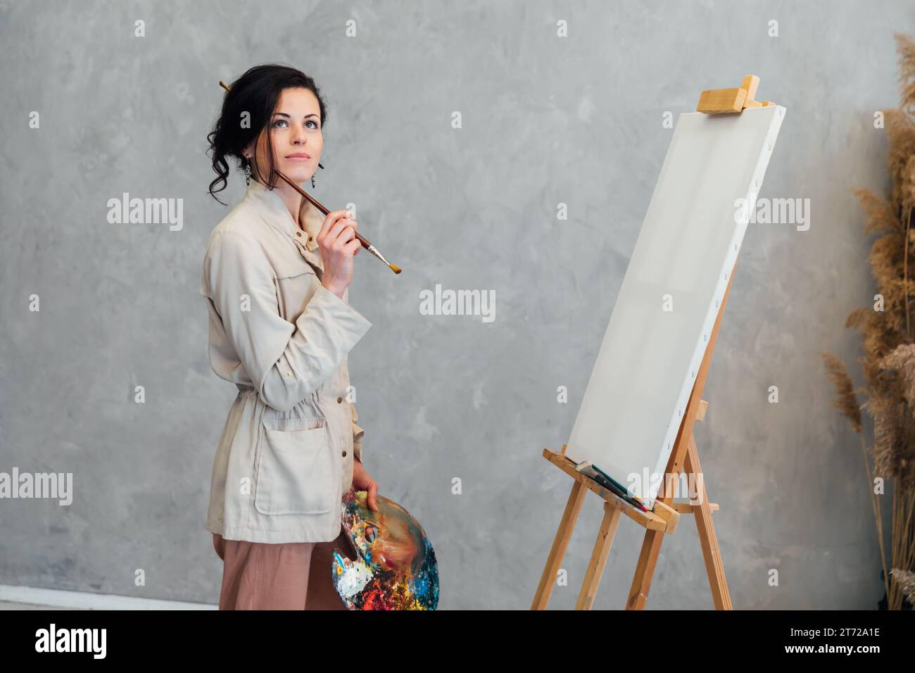a female artist stands at an easel with a brush and is about to paint a ...