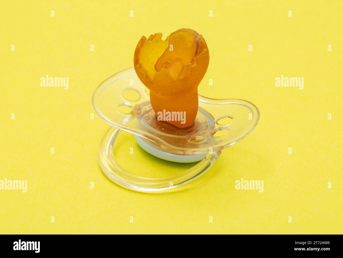 Low-quality torn baby silicone pacifier on a yellow background, close ...