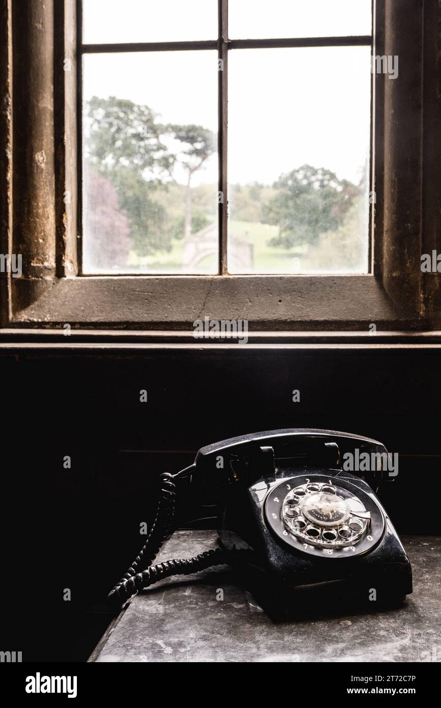 A vintage telephone resting atop a wooden table in front of a window ...