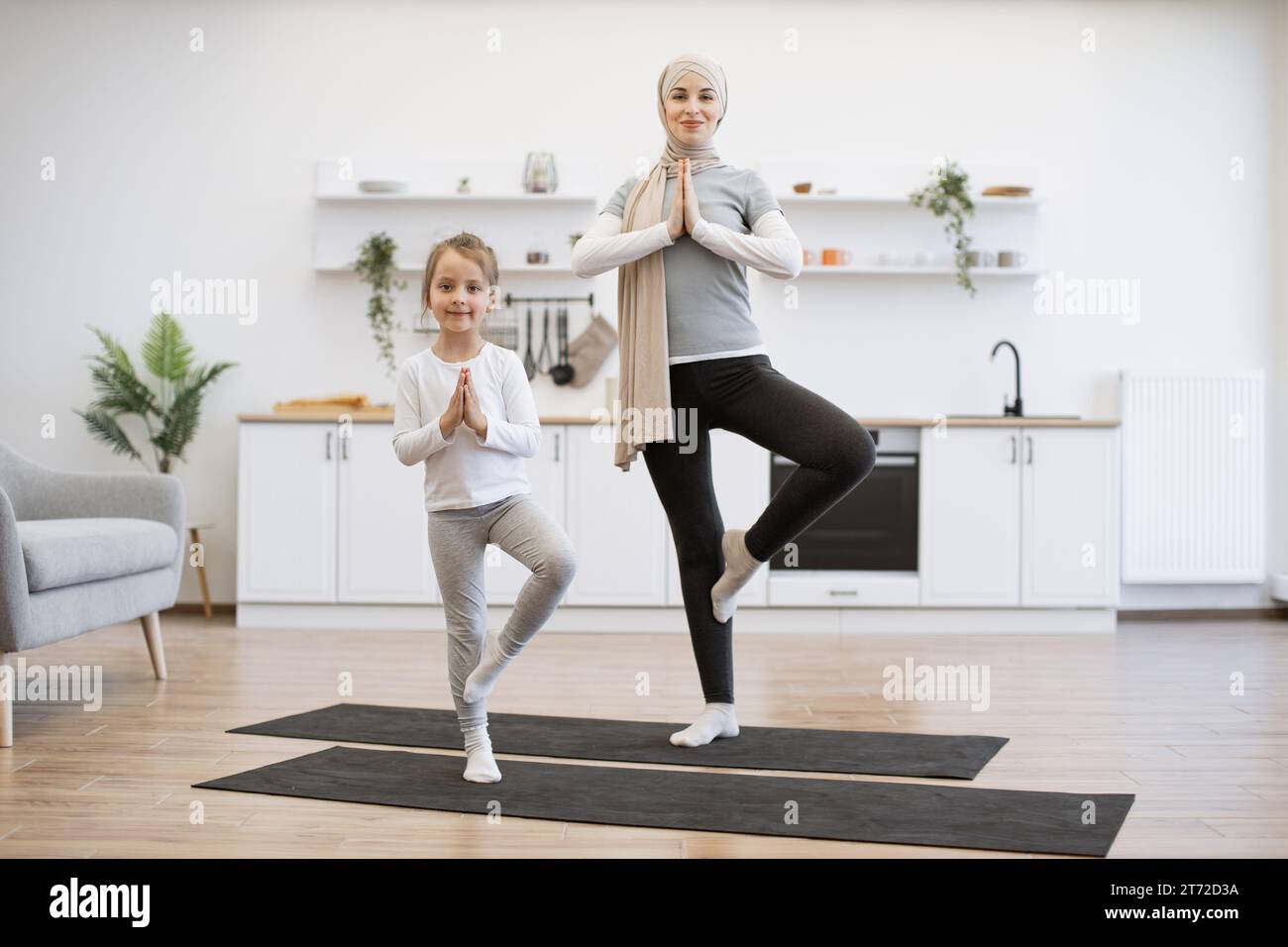 Muslim lady balancing in standing asana with cute girl in sporty outfit ...