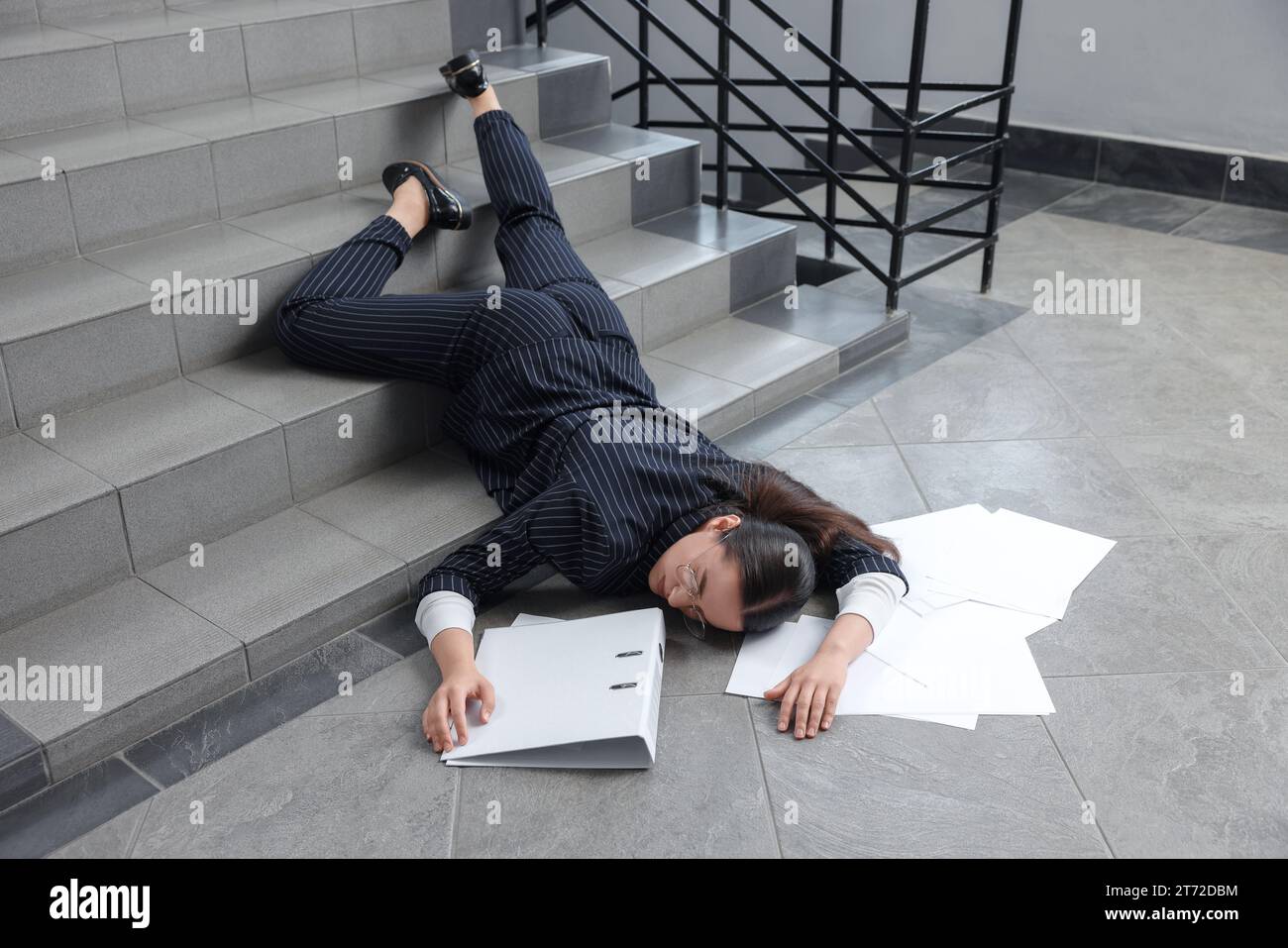 Unconscious woman with scattered folder and papers lying on floor after falling down stairs ...