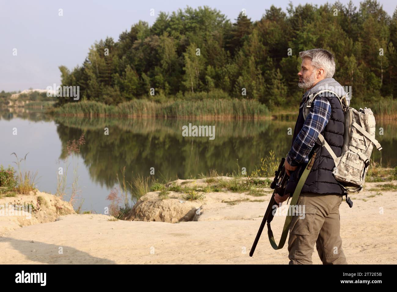 Man with hunting rifle near lake outdoors. Space for text Stock Photo ...