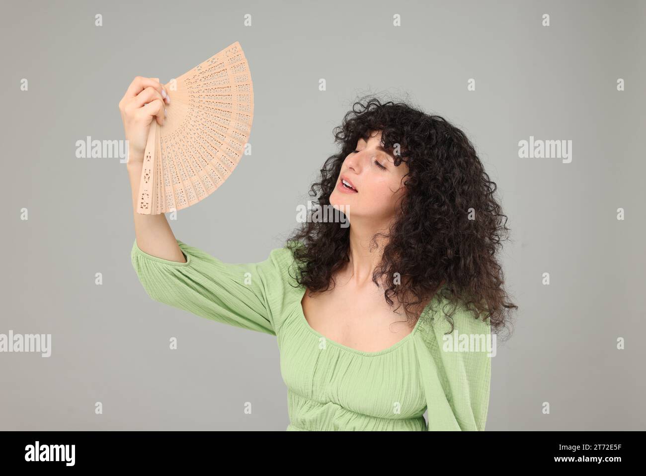 Woman with hand fan suffering from heat on light grey background Stock ...