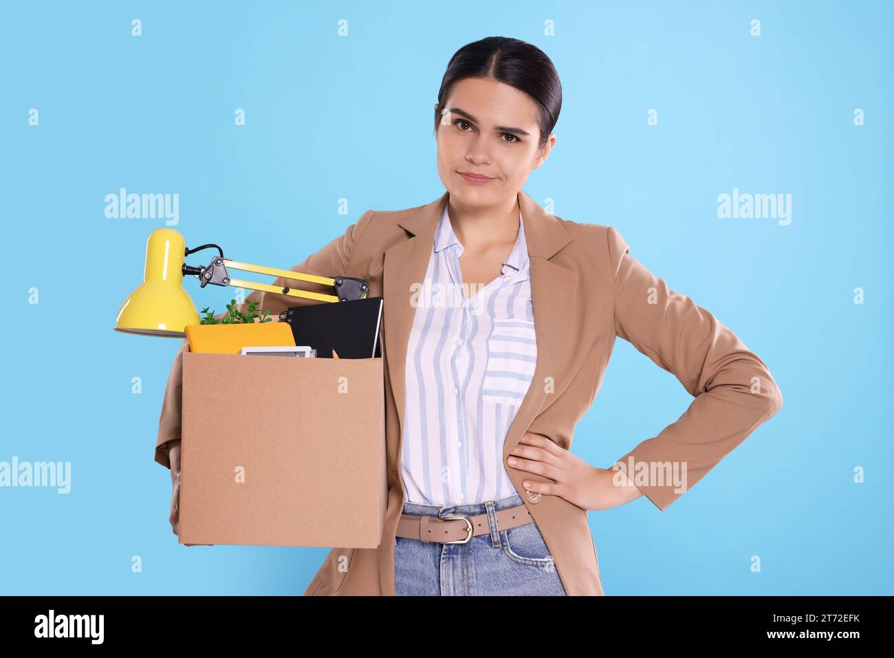 Unemployed woman with box of personal office belongings on light blue ...