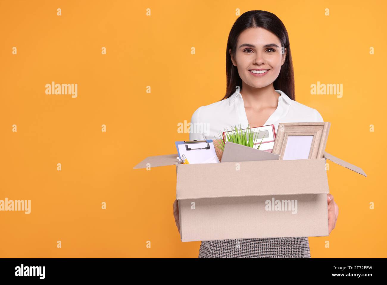 Happy unemployed woman with box of personal office belongings on orange ...