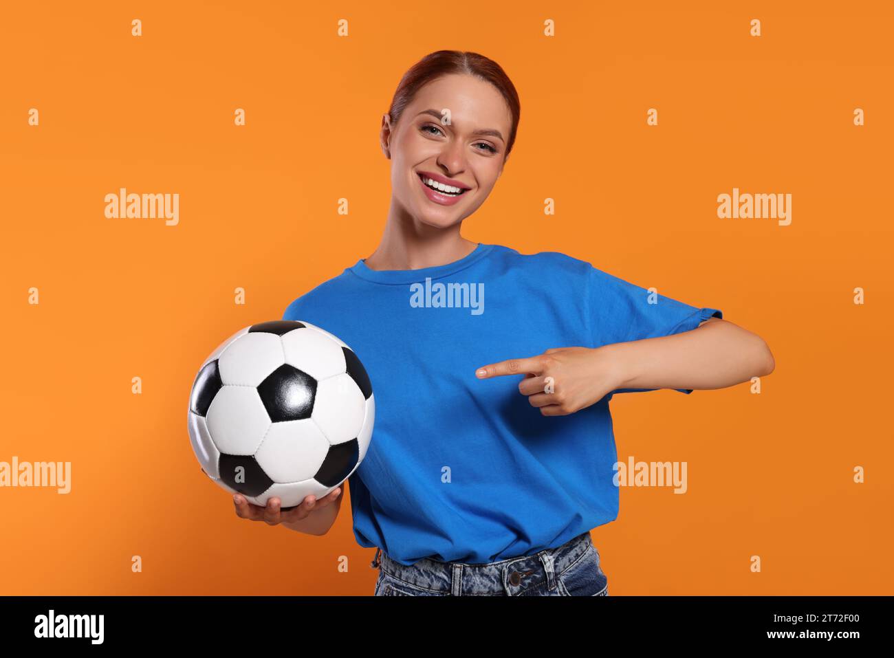 Happy fan showing football ball on orange background Stock Photo - Alamy