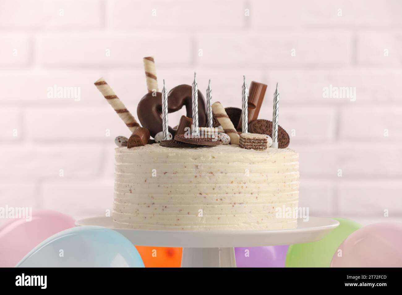 Delicious cake decorated with sweets and candles against white brick ...