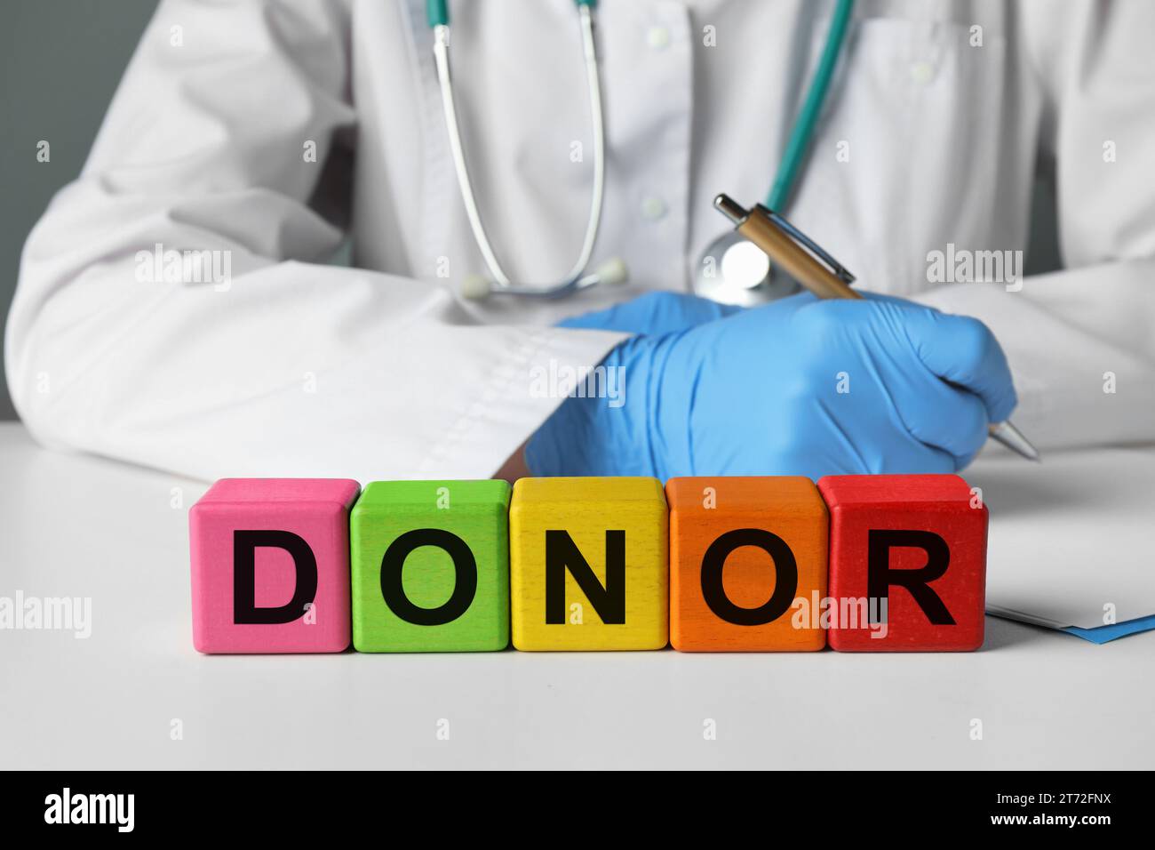 Word Donor made of wooden cubes. Doctor writing in notebook at white ...