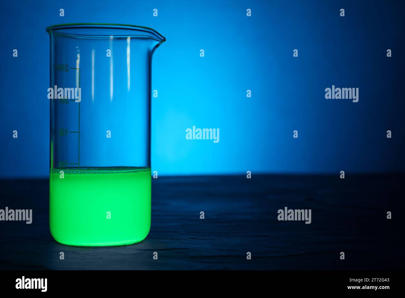 Laboratory beaker with luminous liquid on table against blue background ...