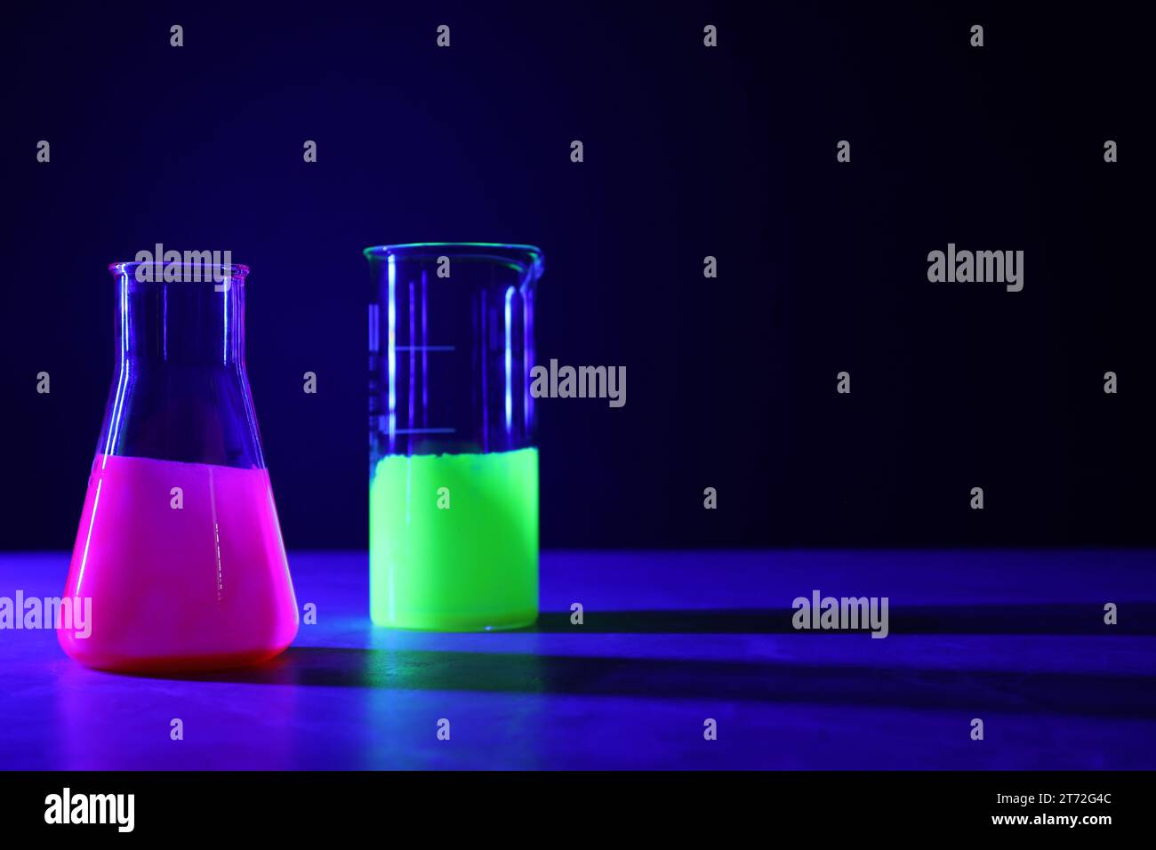 Laboratory glassware with luminous liquids on table against dark ...