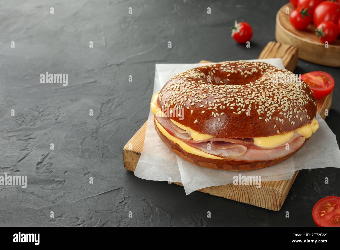 Delicious bagel with ham and cheese on grey textured table, space for ...