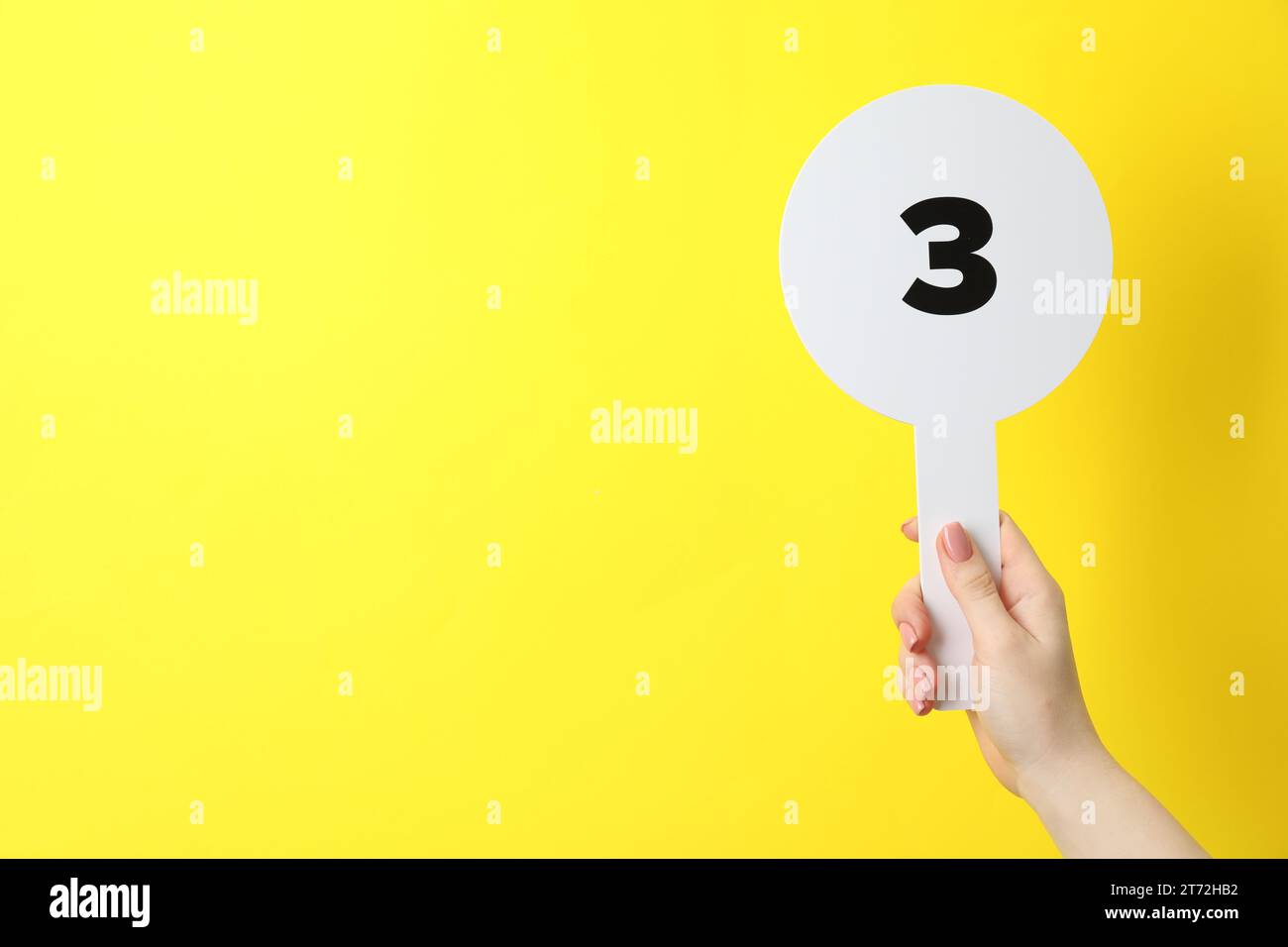 Woman holding auction paddle with number 3 on yellow background ...