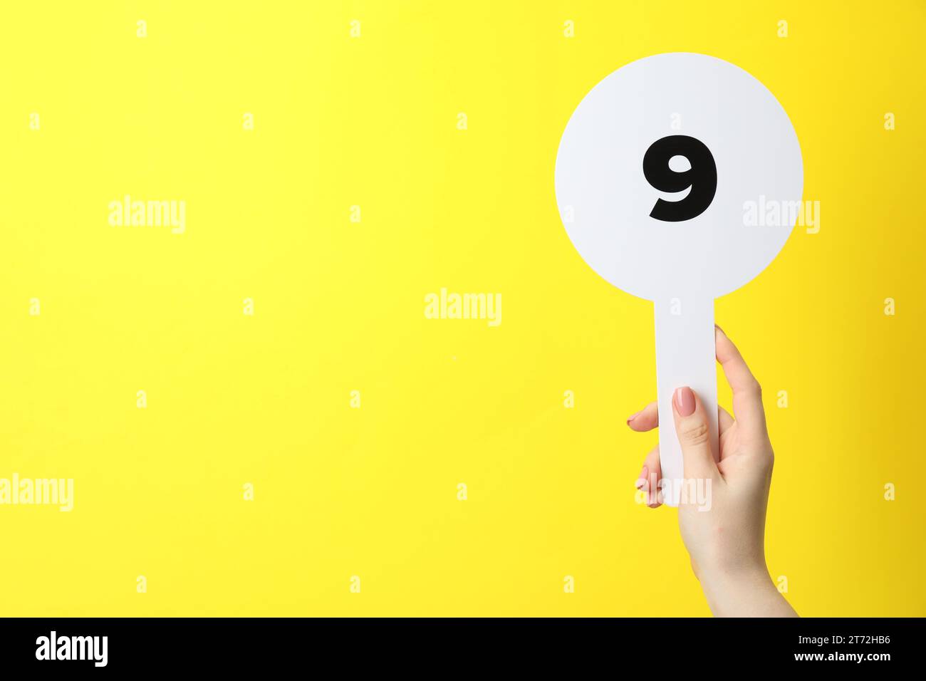 Woman holding auction paddle with number 9 on yellow background ...