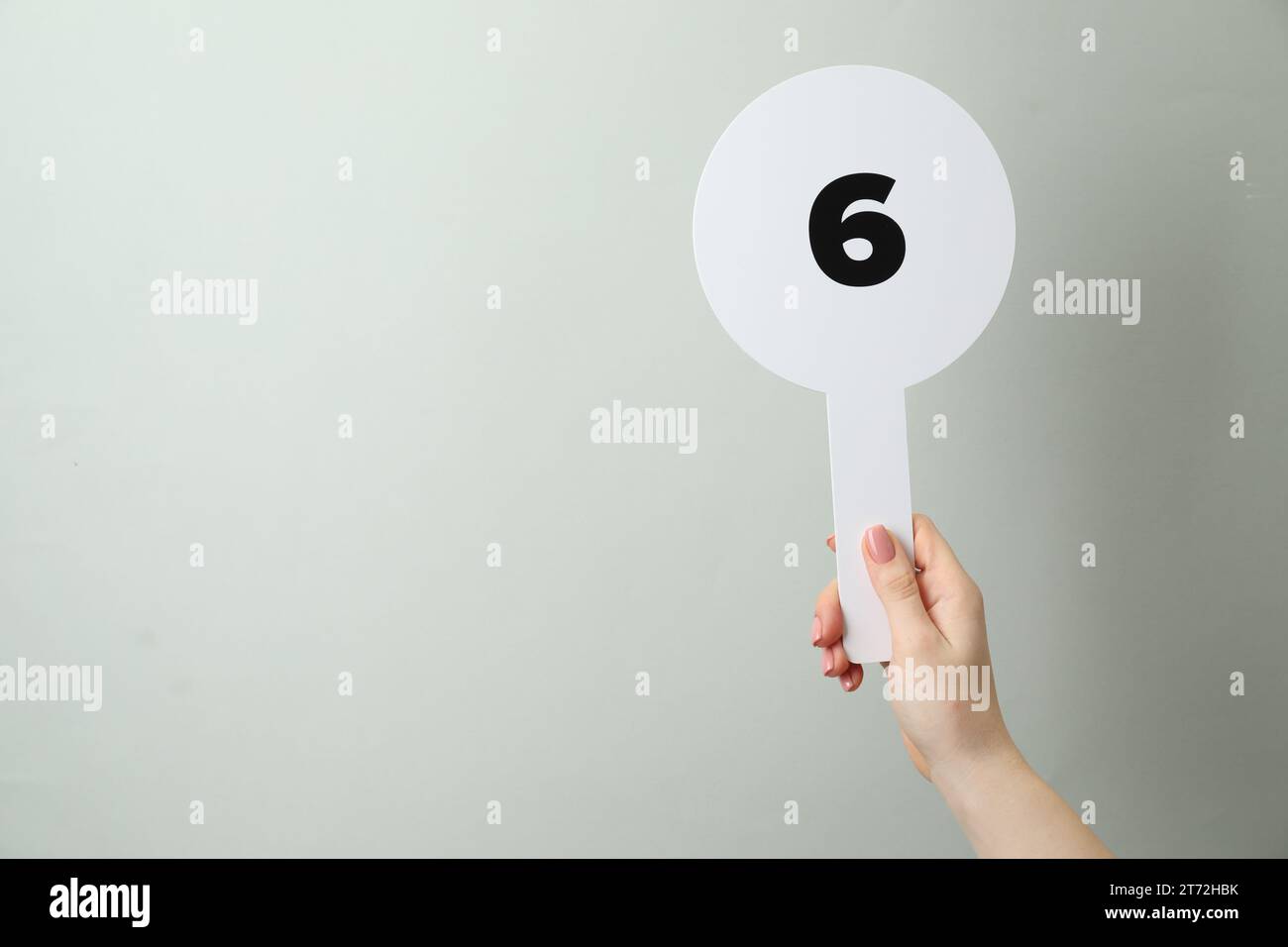 Woman holding auction paddle with number 6 on light grey background ...