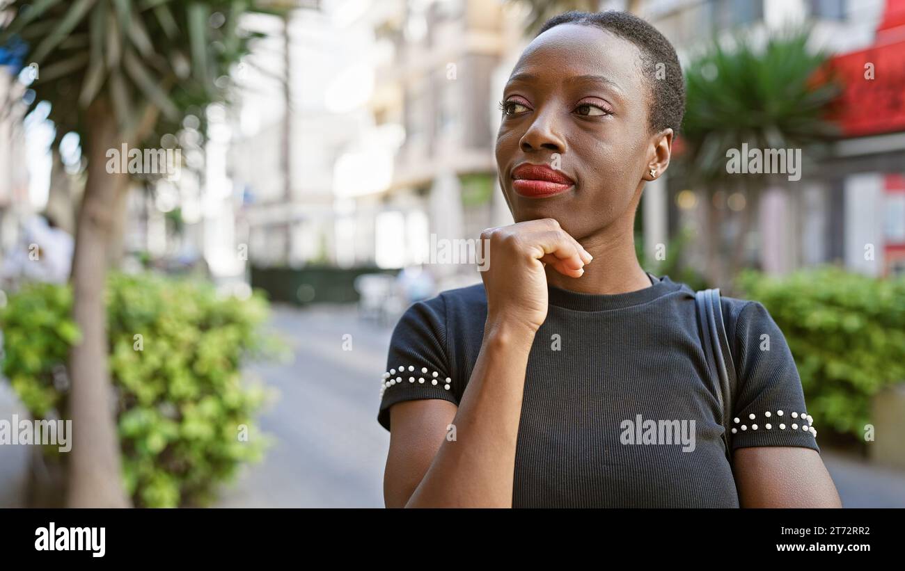 Cool, attractive african american woman standing with a doubtful expression on a sunny city ...